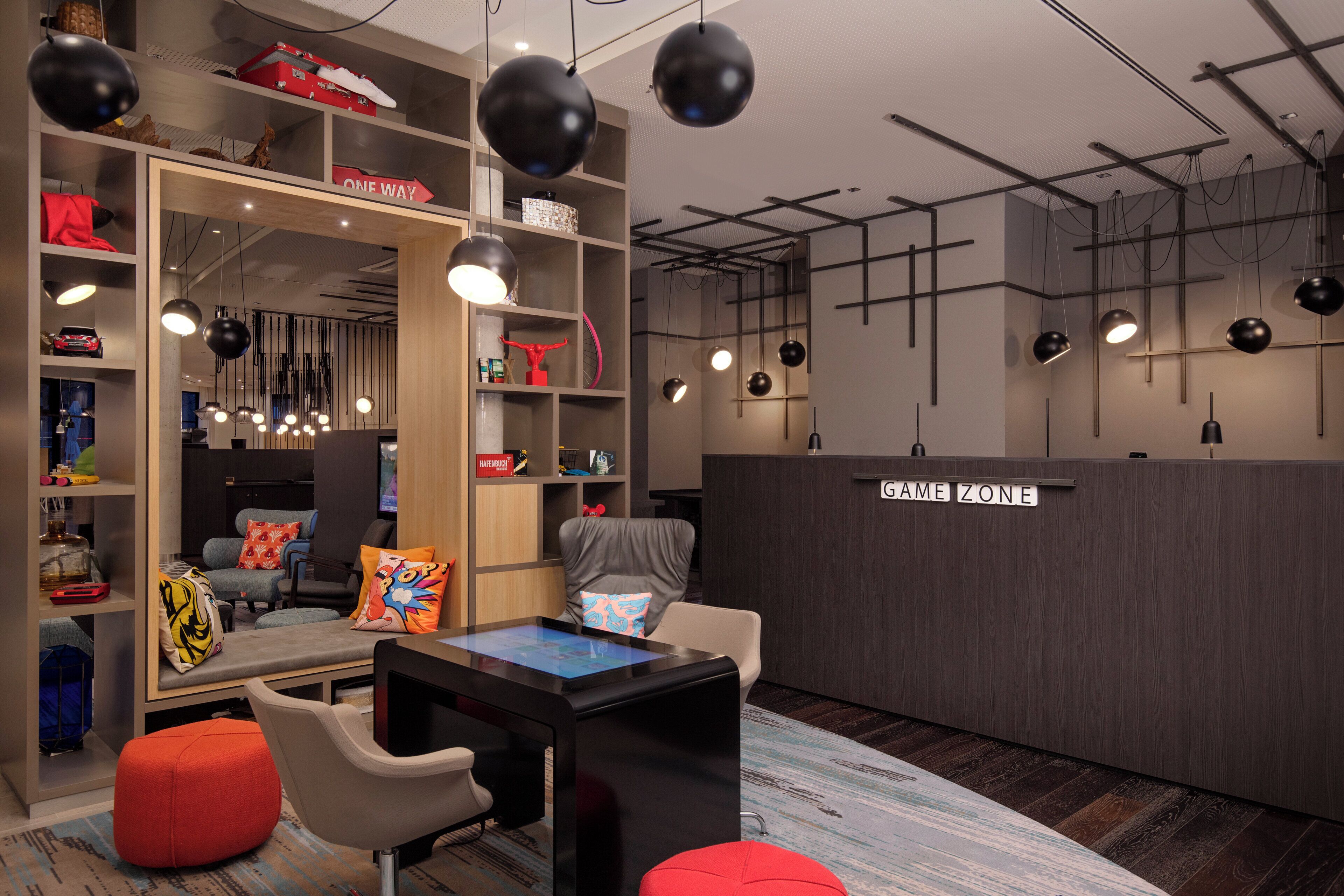 Interior moderno com área de jogos, assentos e uma recepção identificada como 'GAME ZONE'.