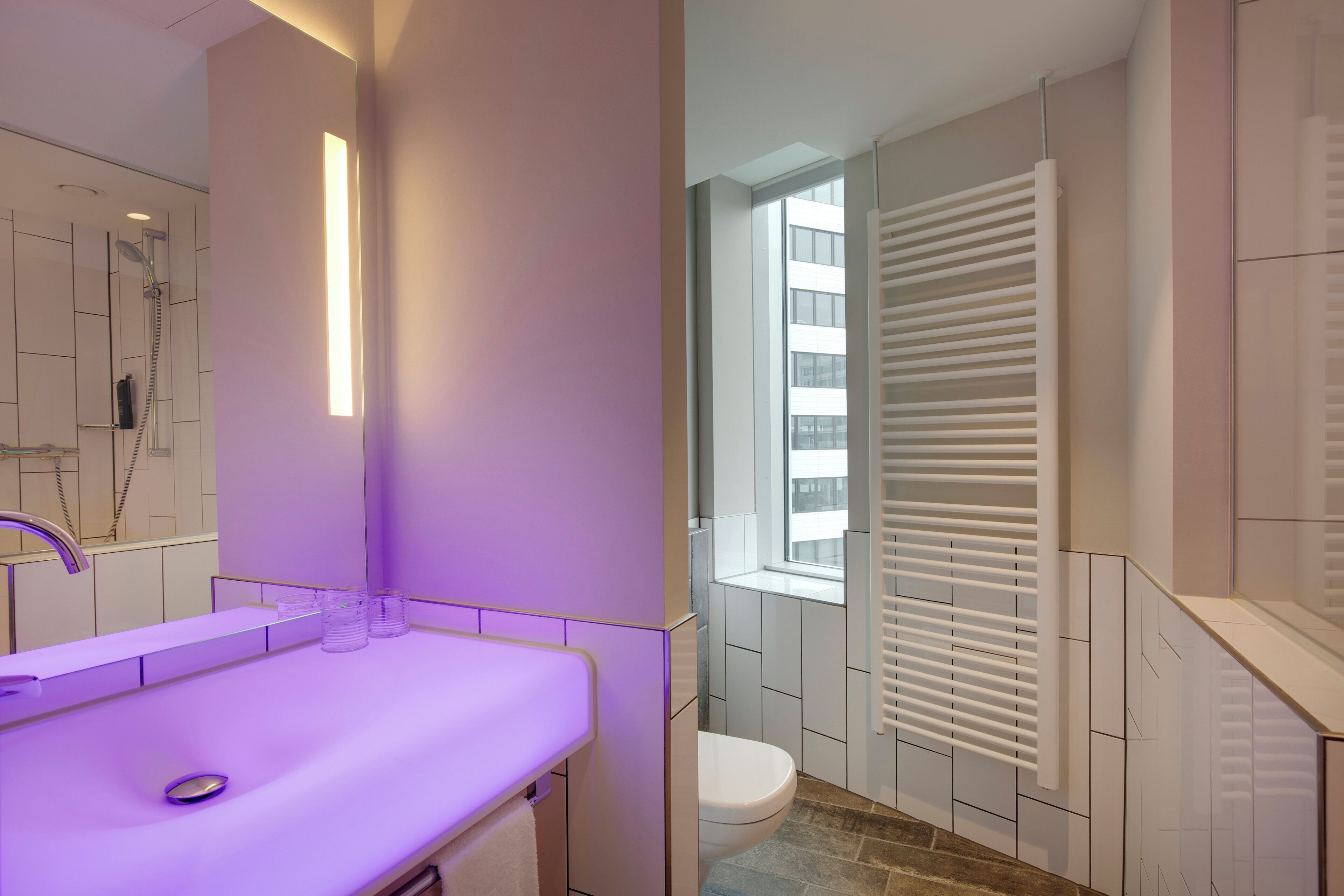 Casa de banho moderna com toucador iluminado em roxo, chuveiro e sanita com vista para a janela.