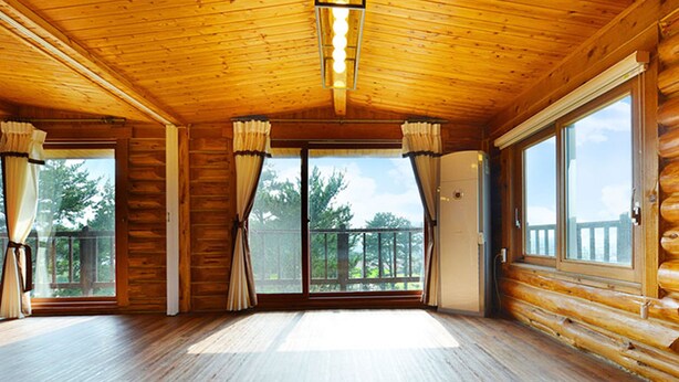Quarto de cabana de tronco com paredes e pisos de madeira, grandes portas de vidro deslizantes e vista para um deck e árvores.