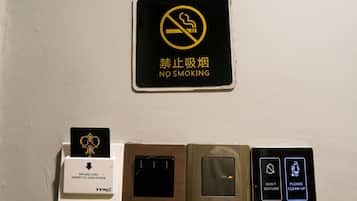 Placa na parede indicando proibido fumar, leitor de cartão para acesso ao quarto e termostato com controle de aquecimento e aquecedor de água.