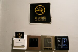 Placa na parede indicando proibido fumar, leitor de cartão para acesso ao quarto e termostato com controle de aquecimento e aquecedor de água.