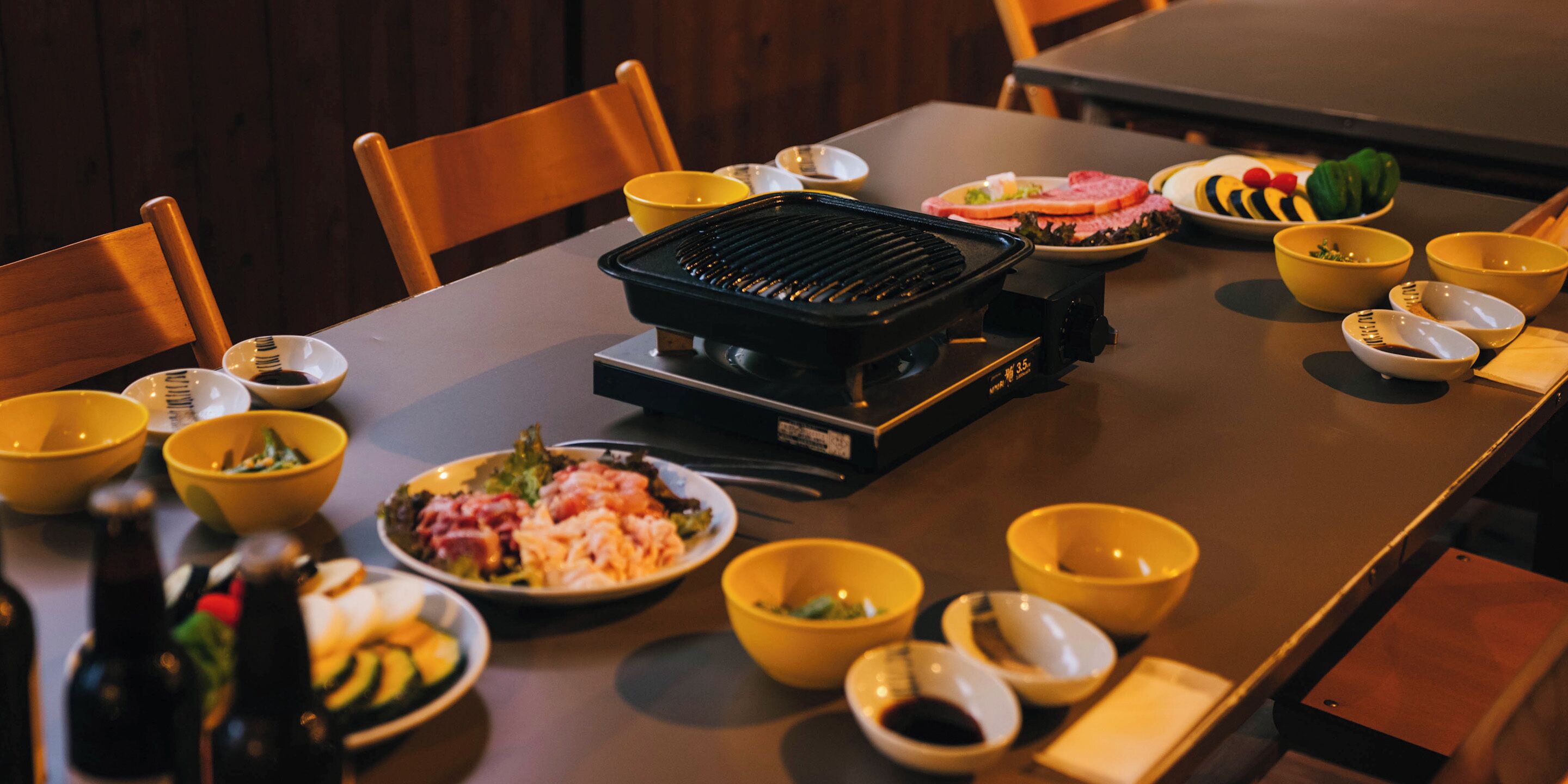 Uma mesa de jantar com uma churrasqueira, diversos pratos e tigelas amarelas.