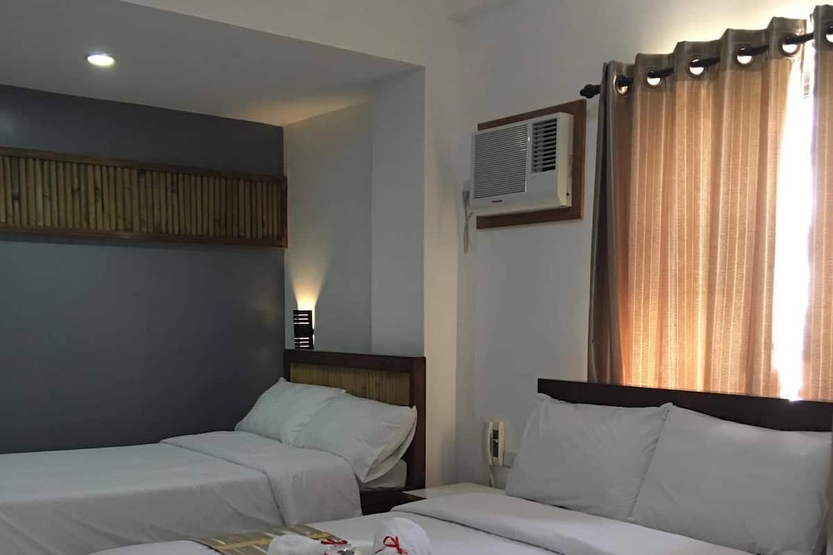 Quarto de hotel com duas camas, cabeceira de madeira, ar condicionado fixado na parede e uma cortina.