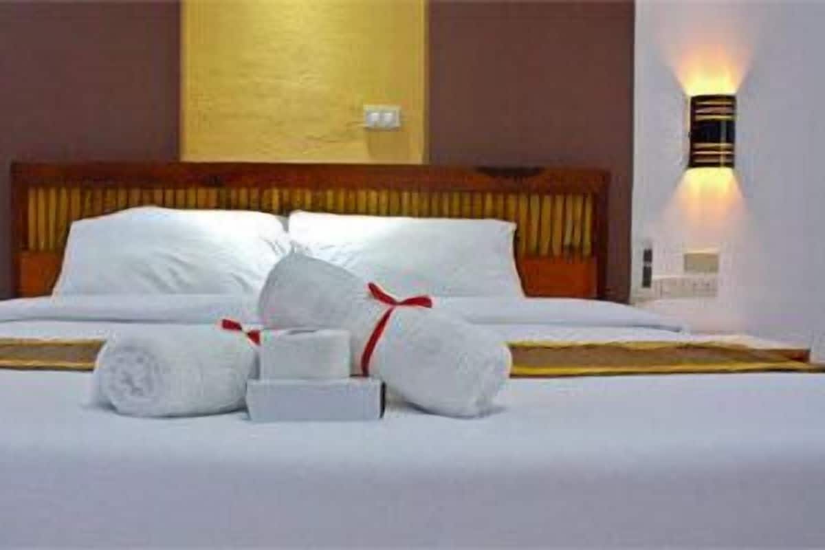 Cama bem arrumada com lençóis brancos, cabeceira de madeira e duas luminárias fixadas na parede.