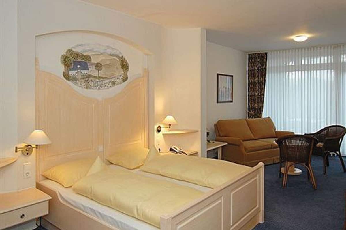 Quarto de hotel com uma cama, mesas de cabeceira, escrivaninha com uma cadeira e um sofá.