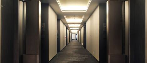 Corredor longo e estreito de um hotel, com carpete e portas em ambos os lados.