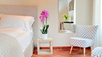 Quarto de hotel com uma cama, uma pequena mesa com uma planta em vaso, uma cadeira e um espelho na parede.