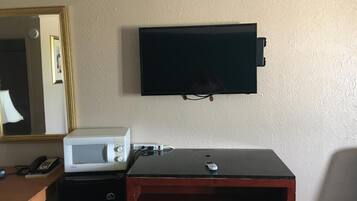 Quarto de hotel com televisão na parede, micro-ondas, telefone e um pequeno armário com gaveta.