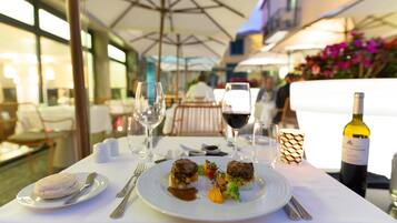 Mesa posta com pratos, talheres e uma garrafa de vinho, com vista para a área de estar externa.
