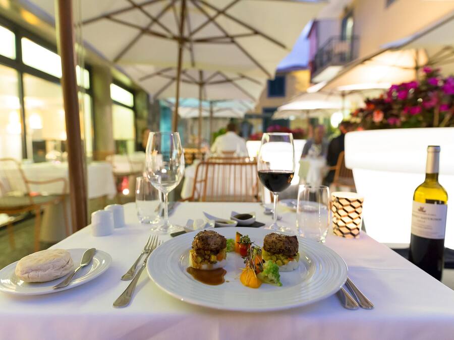 Mesa posta com pratos, talheres e uma garrafa de vinho, com vista para a área de estar externa.
