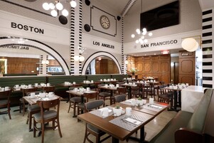 Um restaurante com cabines e mesas, placas com Boston, Los Angeles e São Francisco, e um relógio na parede.