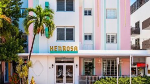 Um edifício de vários andares com fachada rosa e branca, uma entrada visível e uma placa com a inscrição 'HEÑROSA'.