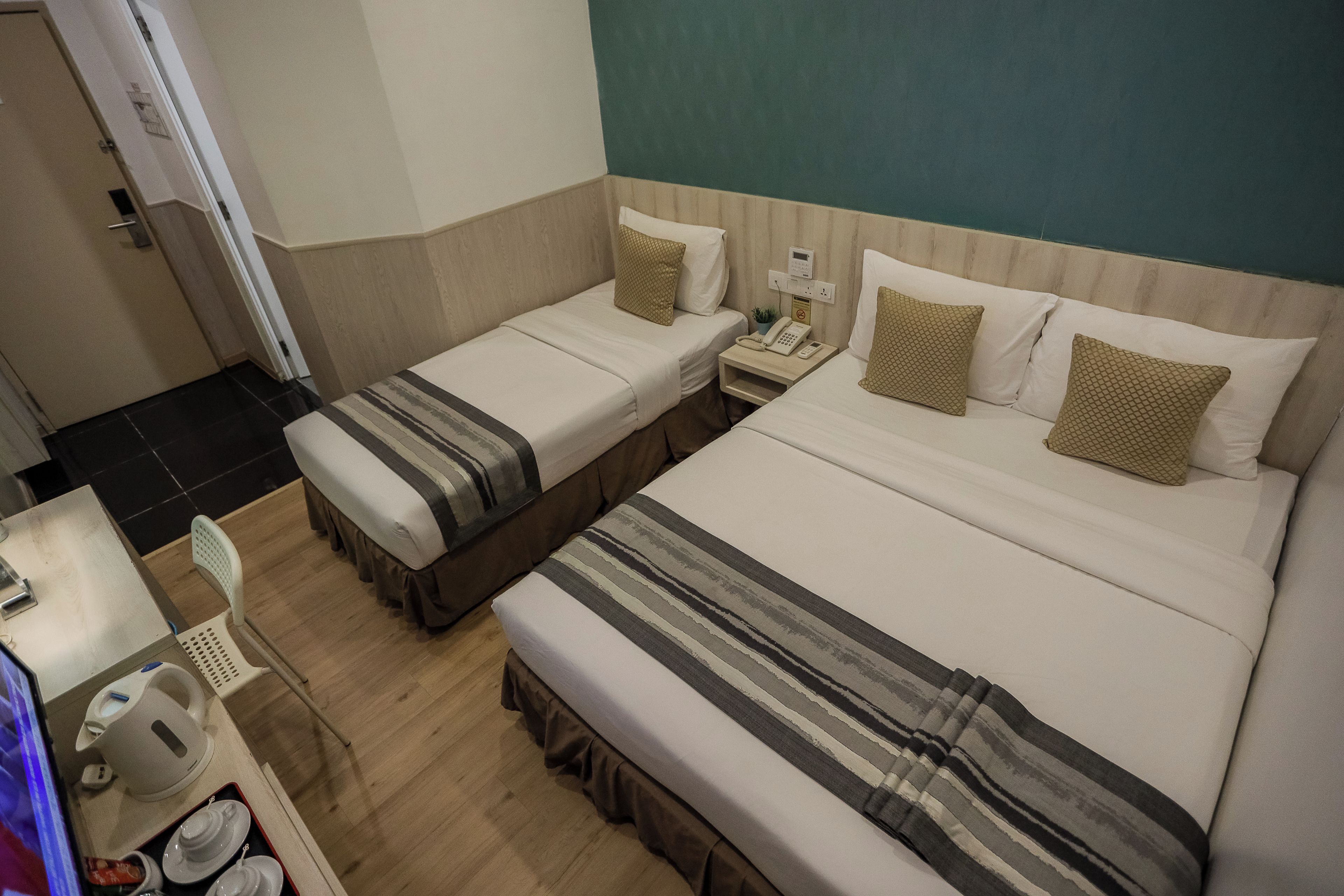 Quarto de hotel com duas camas de solteiro, uma cama de casal, mesa de cabeceira com telefone e pequena escrivaninha com cadeira.