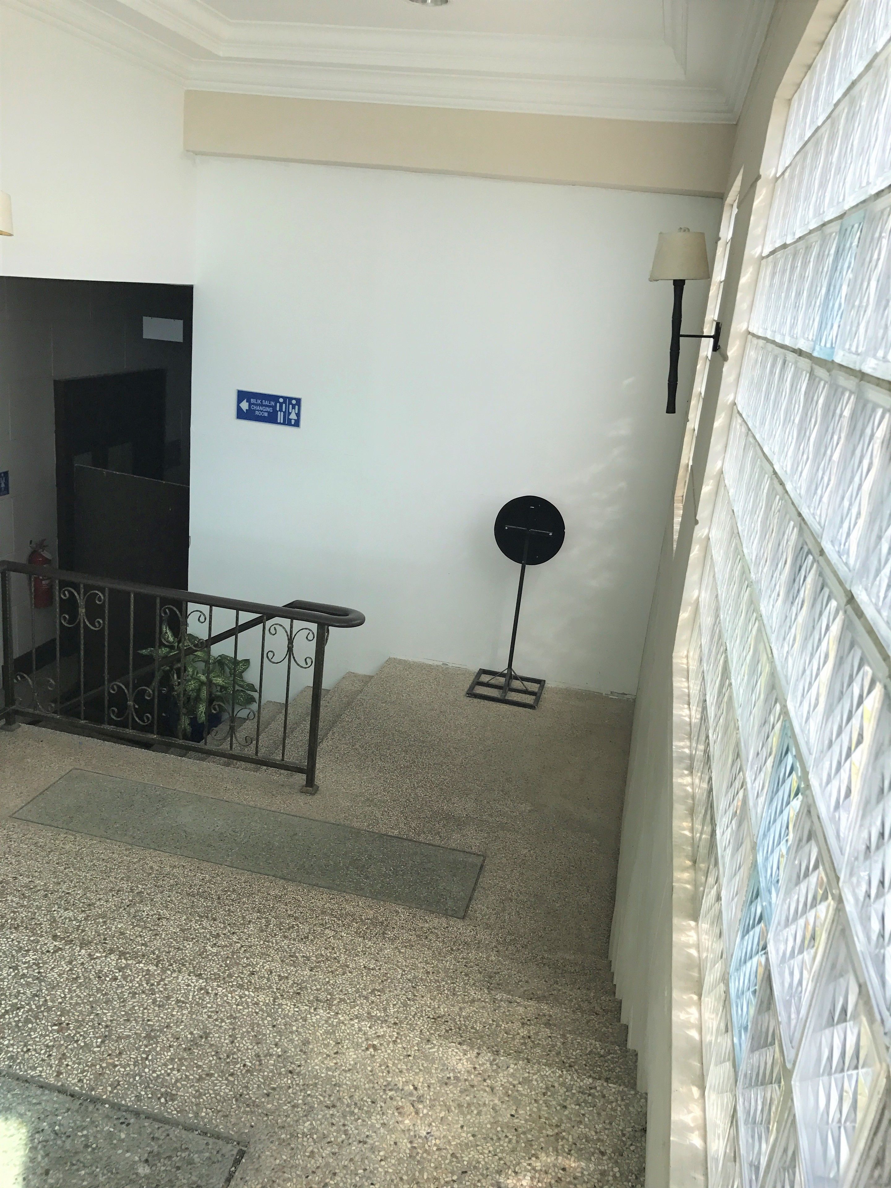 Uma escadaria com corrimão, uma placa indicando um quarto e um abajur fixado na parede.