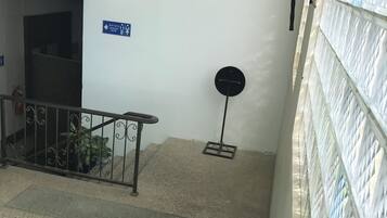 Uma escadaria com corrimão, uma placa indicando um quarto e um abajur fixado na parede.