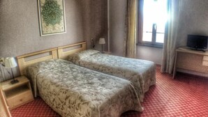 Quarto com duas camas, uma escrivaninha, uma luminária e uma televisão.