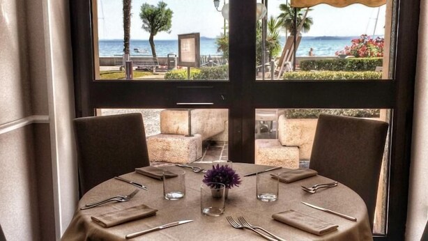 Mesa de jantar posta para dois, com vista para o mar através de uma janela.