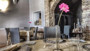 Interior de restaurante com paredes de pedra, mesas montadas com pratos, copos e talheres.