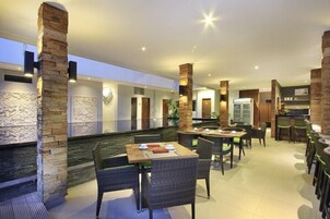 Um hall de hotel moderno com pilares de pedra, mobiliário de vime e uma área de recepção.