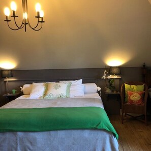 Uma cama bem arrumada com um edredom verde, um lustre e duas luminárias laterais.