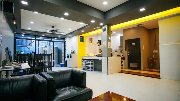 Uma sala de estar moderna com um sofá de couro preto, uma mesa de centro de madeira e uma área de refeições com cozinha ao fundo.