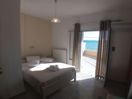 Quarto com cama, radiador, janela com cortinas e vista para o mar.