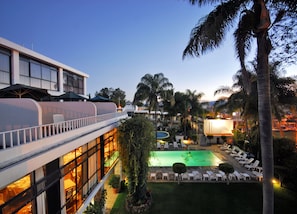 Hotel com piscina, espreguiçadeiras e palmeiras.