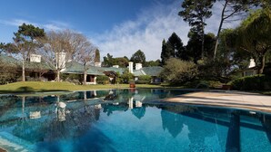Piscina cristalina com um deck de madeira, rodeada por vegetação exuberante e diversas árvores.