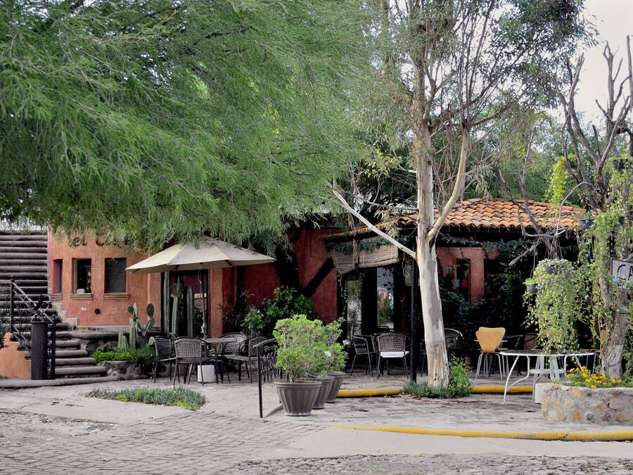 Uma área de pátio externo com mesas e cadeiras, uma escadaria e um edifício com fachada vermelha.
