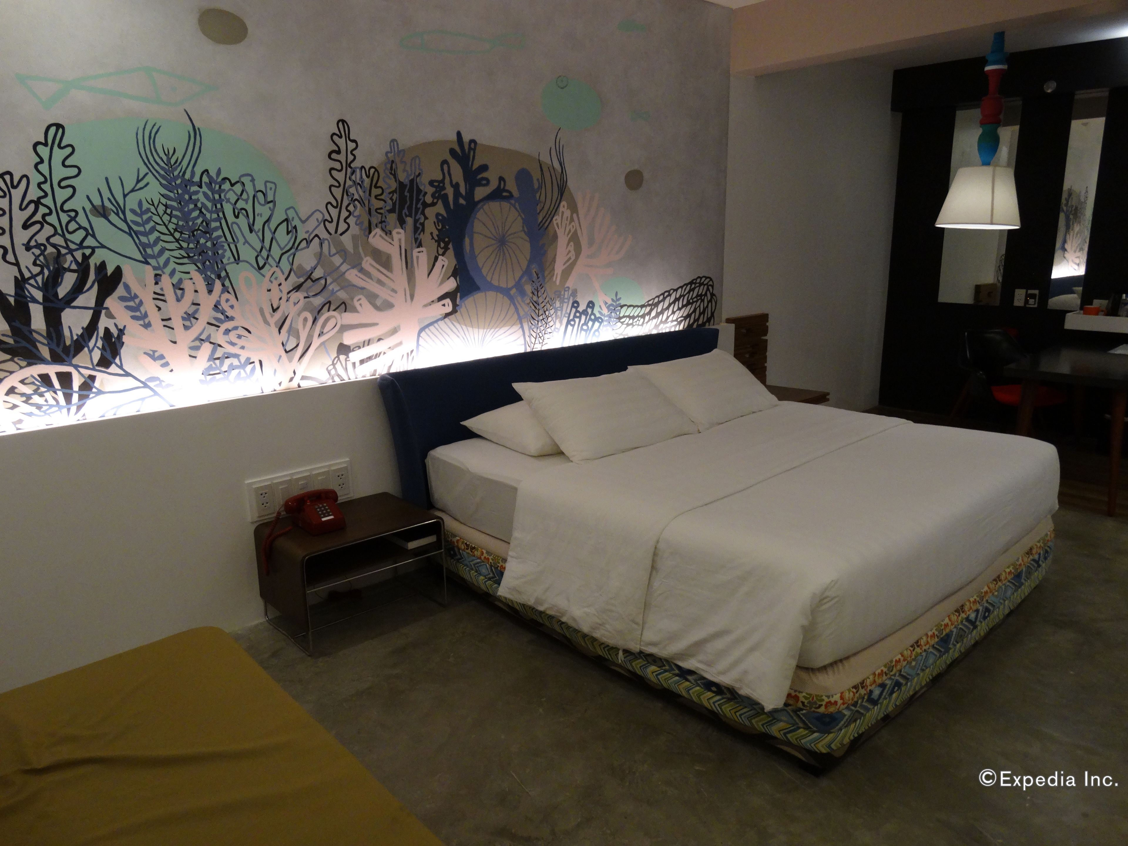 Um quarto com cama, mesa de cabeceira, painel decorativo na parede e escrivaninha com cadeira.