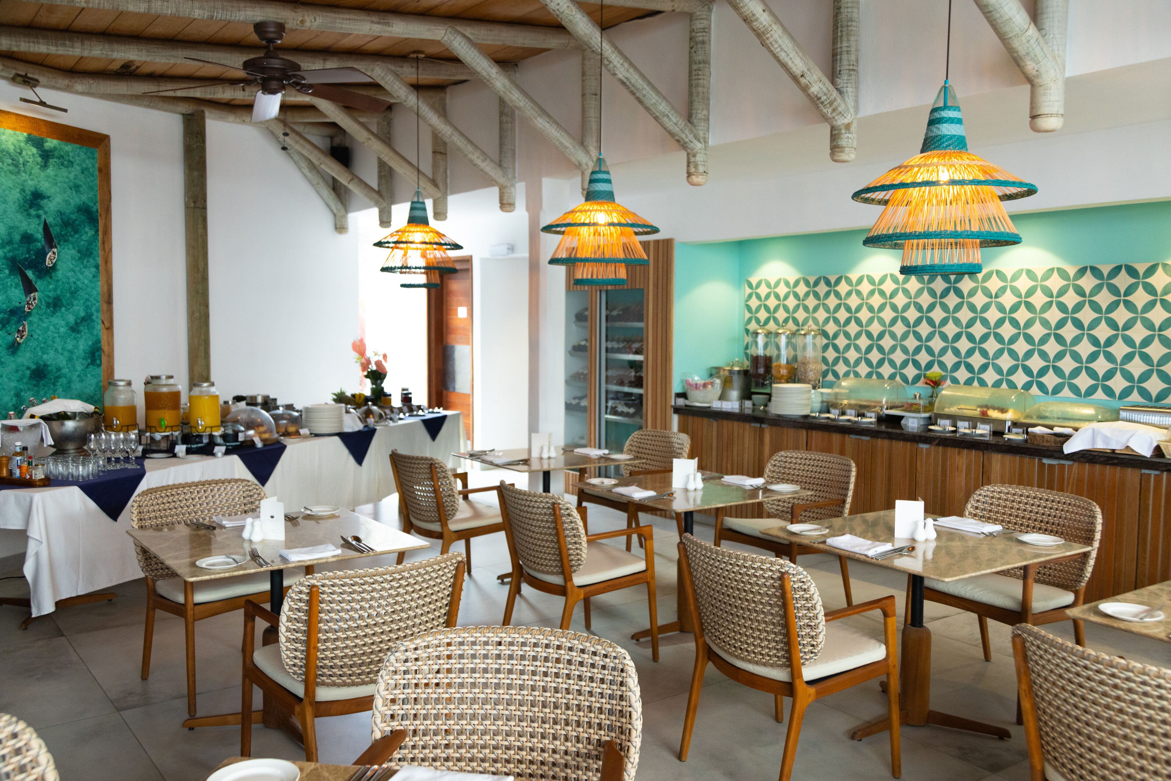 Um restaurante com cadeiras e mesas de vime, luminárias pendentes de vime e um painel de parede estampado.
