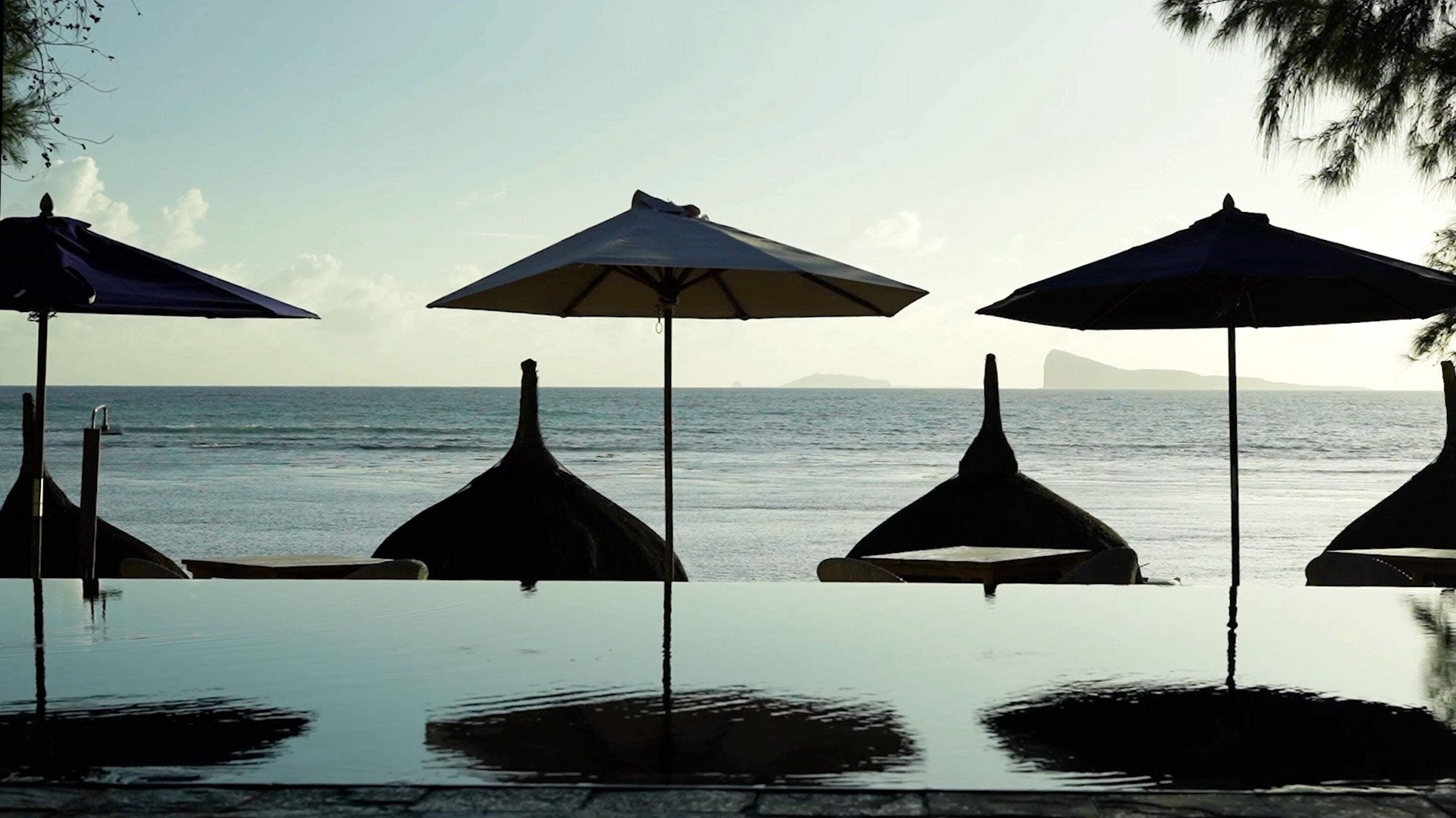 Área à beira da piscina com guarda-sóis e espreguiçadeiras, com vista para o mar.