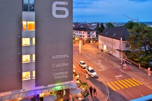 Um hotel com um grande letreiro com o número '6', um café/bar e música ao vivo/dança.