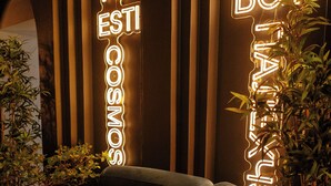 Uma área de estar moderna com um letreiro de neon que diz “TU COSMOS” e “BOY BOY” em uma fonte elegante.