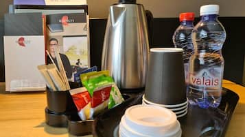 Bandeja de café da manhã com cafeteira, garrafas de água, caneca e lanches embalados.