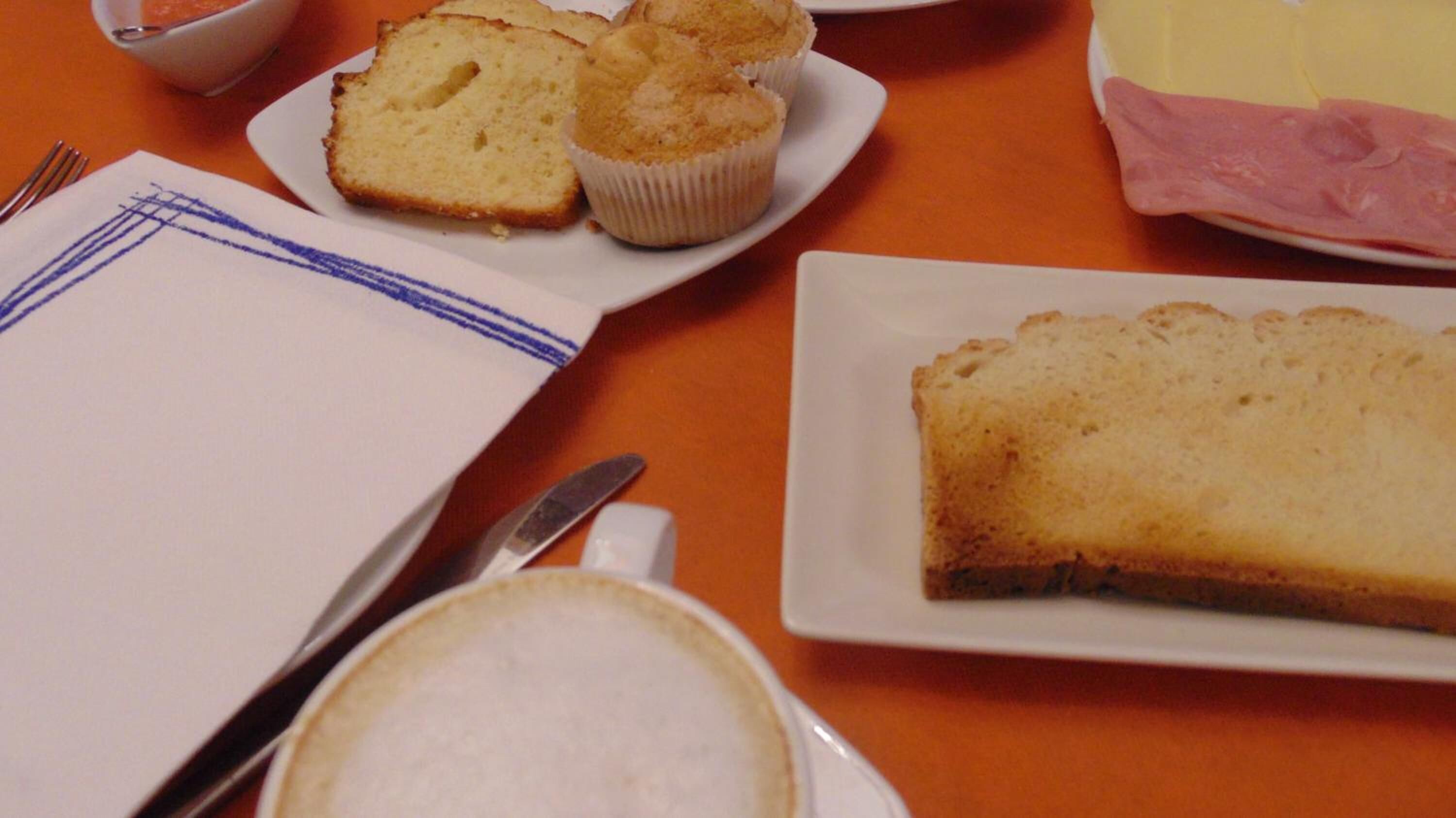 Uma mesa com um prato de bolo, um prato de muffins e um prato de presunto.