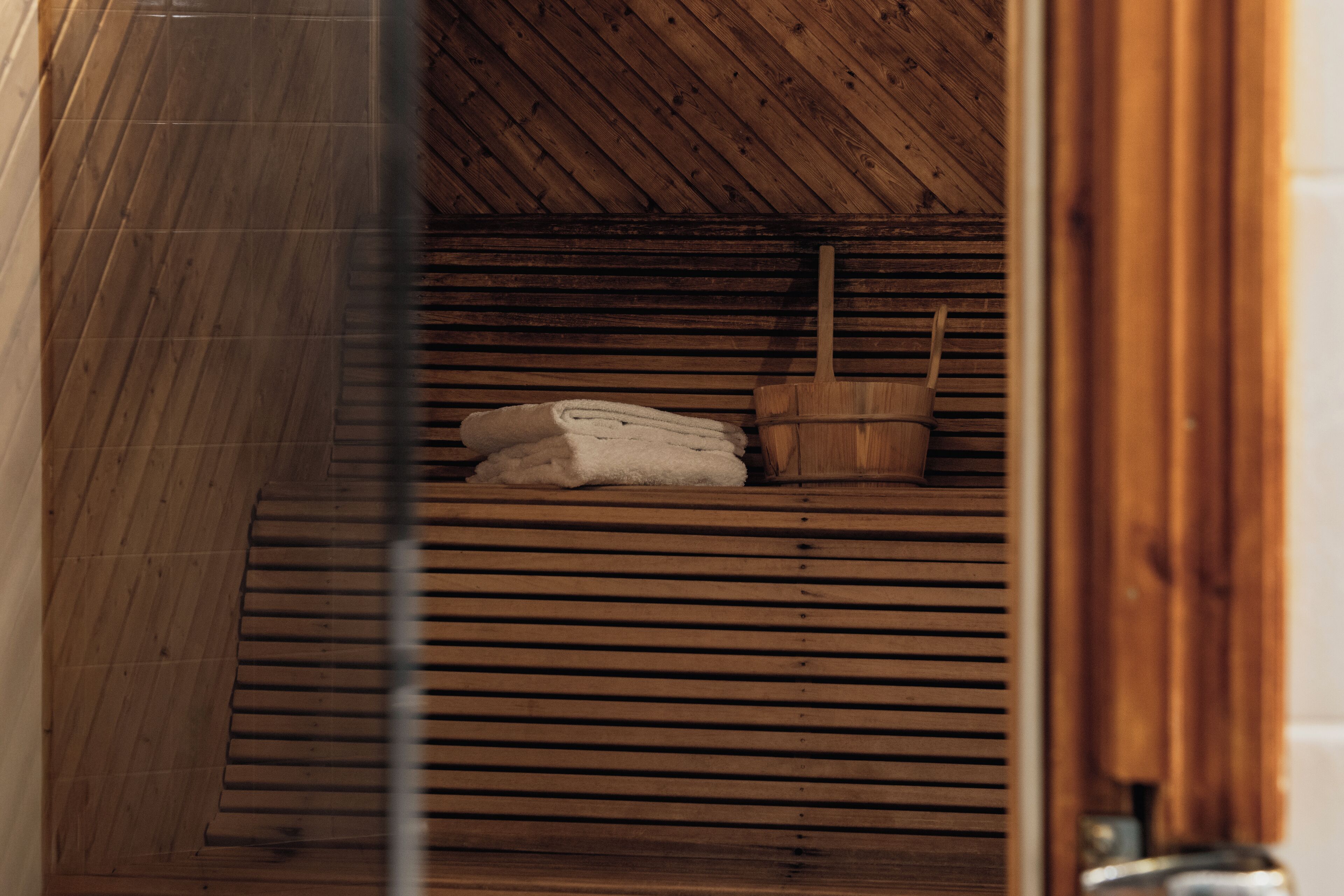 Uma sala de sauna com ripas de madeira, uma toalha e um balde de madeira.