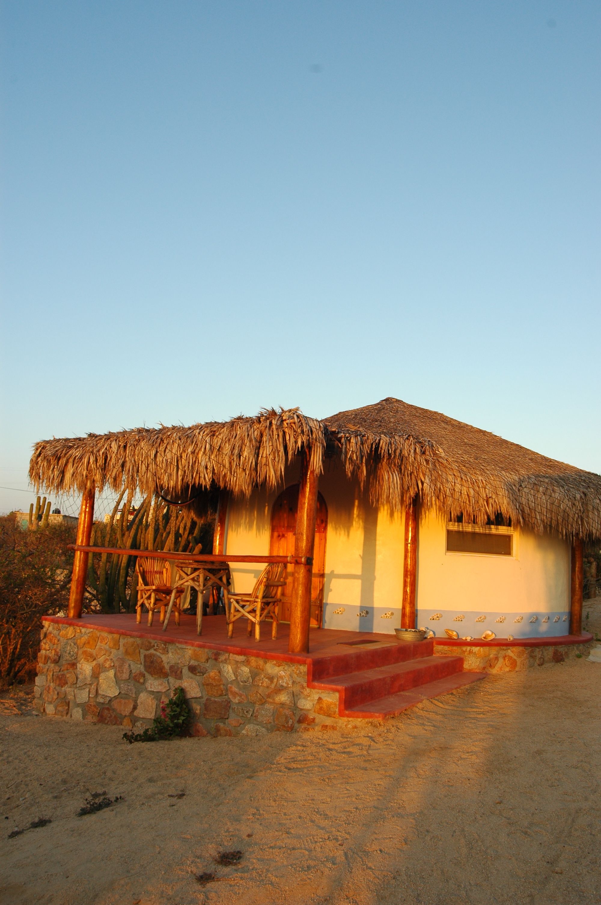 Um edifício rústico com telhado de palha, degraus de pedra e varanda de madeira.