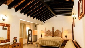 Quarto com teto de madeira, cama com cabeceira estampada, abajures e cômoda de madeira.