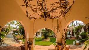 Um corredor em arco com vista para um jardim, apresentando uma fonte central e plantas em vasos.