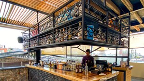 Uma área de bar com balcão de madeira, prateleiras com garrafas e piso ladrilhado.