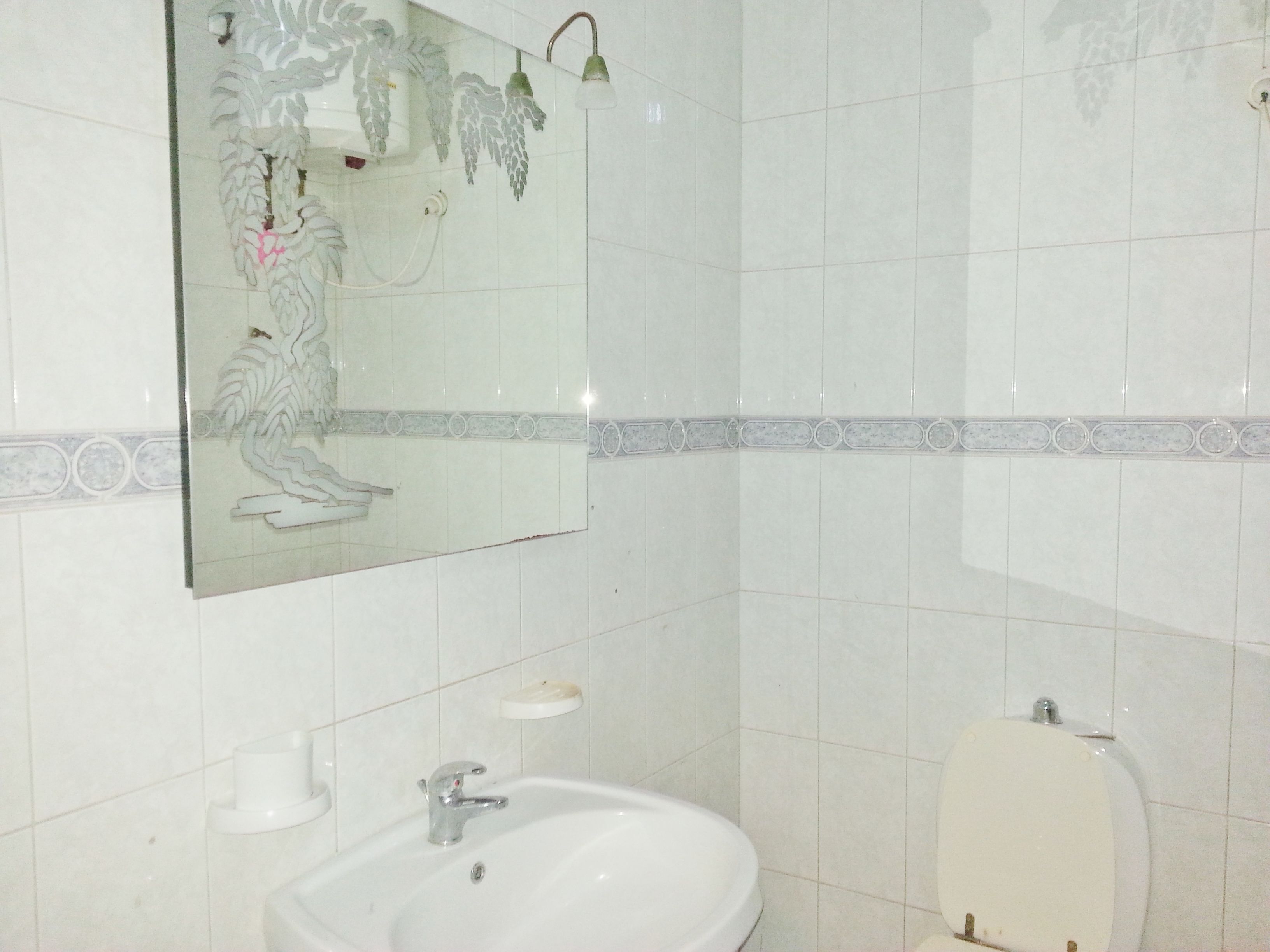 Casa de banho com lavatório branco, espelho e sanita.