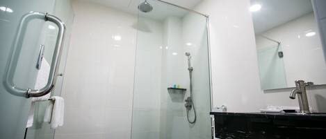 Um banheiro moderno com chuveiro em box de vidro, bancada preta e pia branca.
