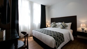 Quarto de hotel com uma cama grande, uma escrivaninha e uma televisão.
