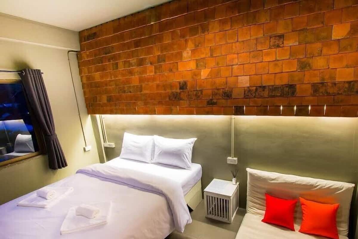 Quarto de hotel com cabeceira em padrão de tijolos, cama com lençóis brancos, mesa de cabeceira com abajur e janela com cortinas.