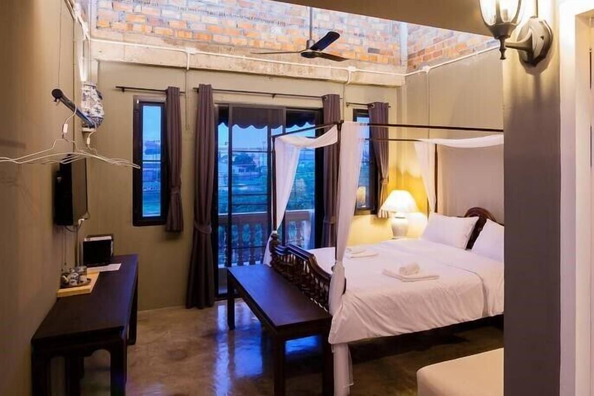 Quarto de hotel com cama, escrivaninha, cadeira, varanda com cortinas e ventilador de teto.