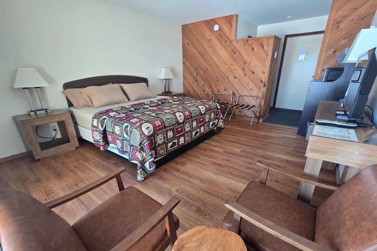 Quarto com cama, duas mesinhas de cabeceira, escrivaninha e cadeira.