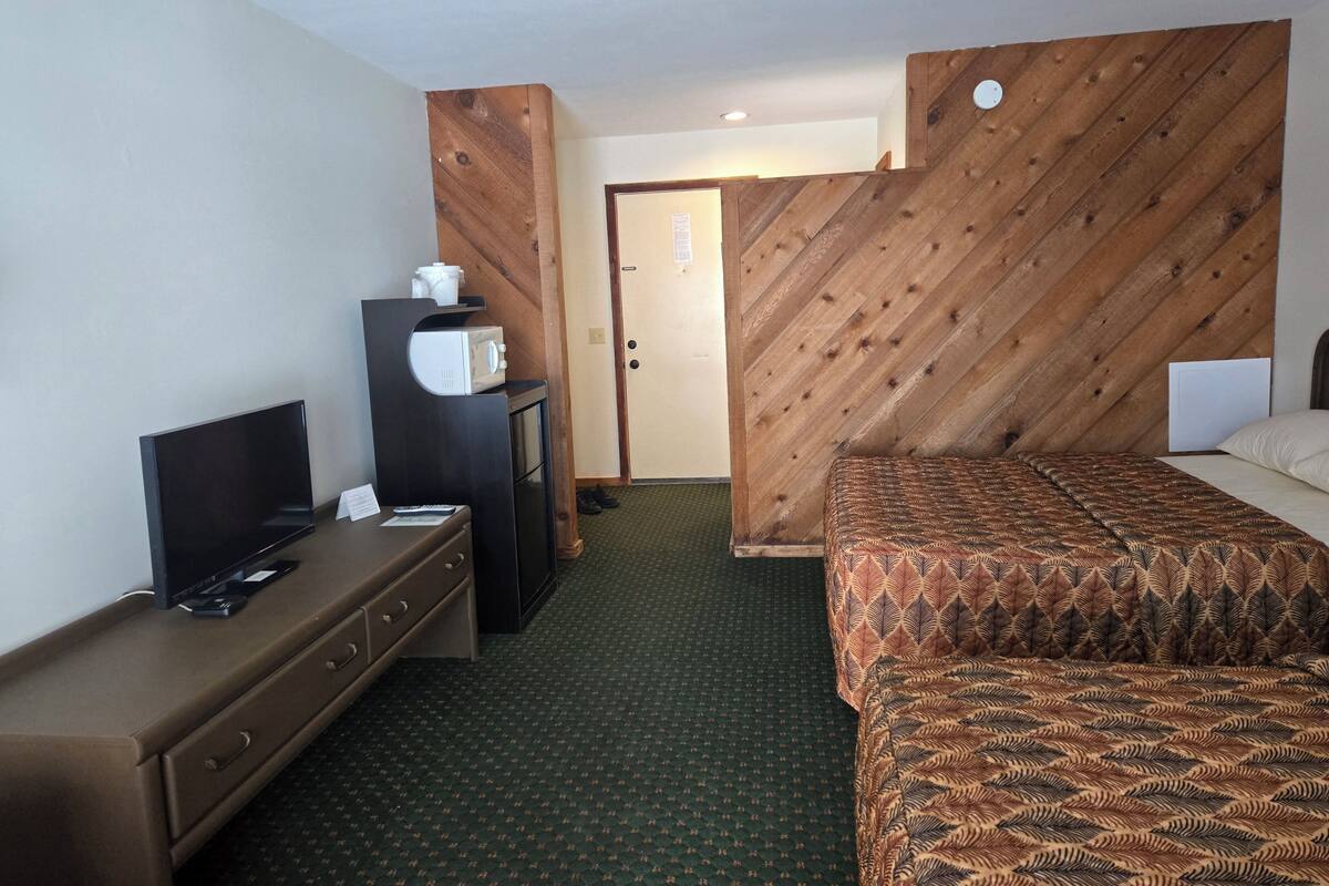 Quarto de hotel com cama, televisão, escrivaninha e micro-ondas.