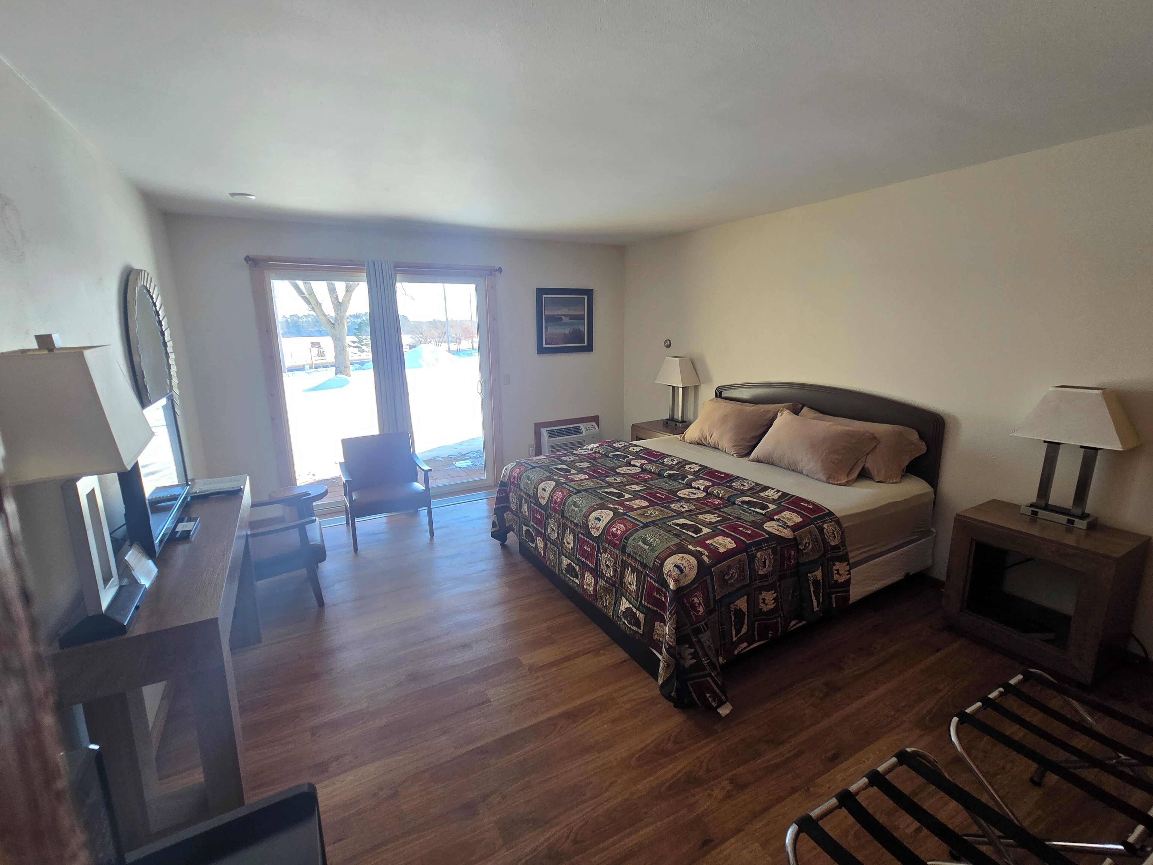 Quarto de hotel com cama, escrivaninha, cadeira e janela.