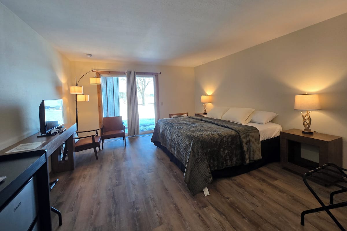 Quarto de hotel com uma cama, uma escrivaninha com computador, uma cadeira e um abajur.